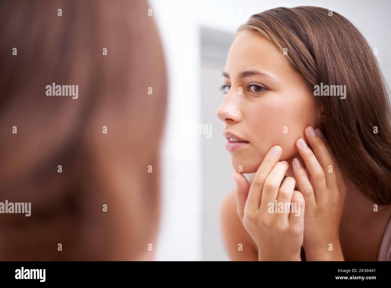 Searching for imperfections. A young woman examining her face in the ...