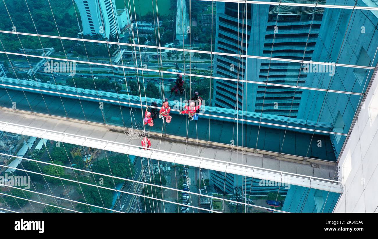 Window cleaning workers hanging outside blue glass office building ...