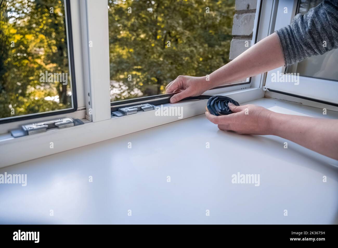 Preparing for the cold season. A woman sticks a dark rubber sealing ...