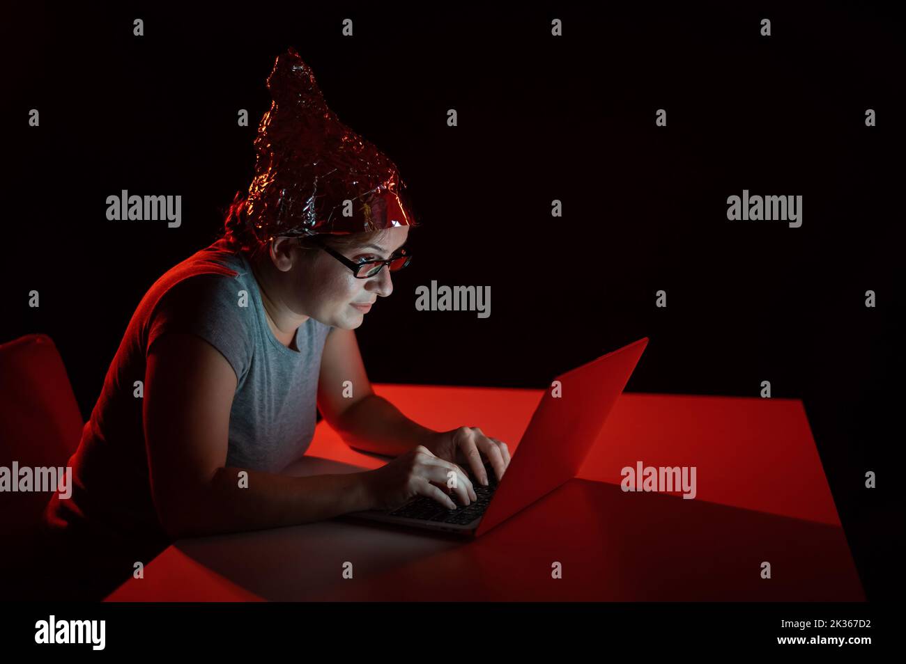 Paranoid caucasian woman typing on a computer wearing a tinfoil cap ...