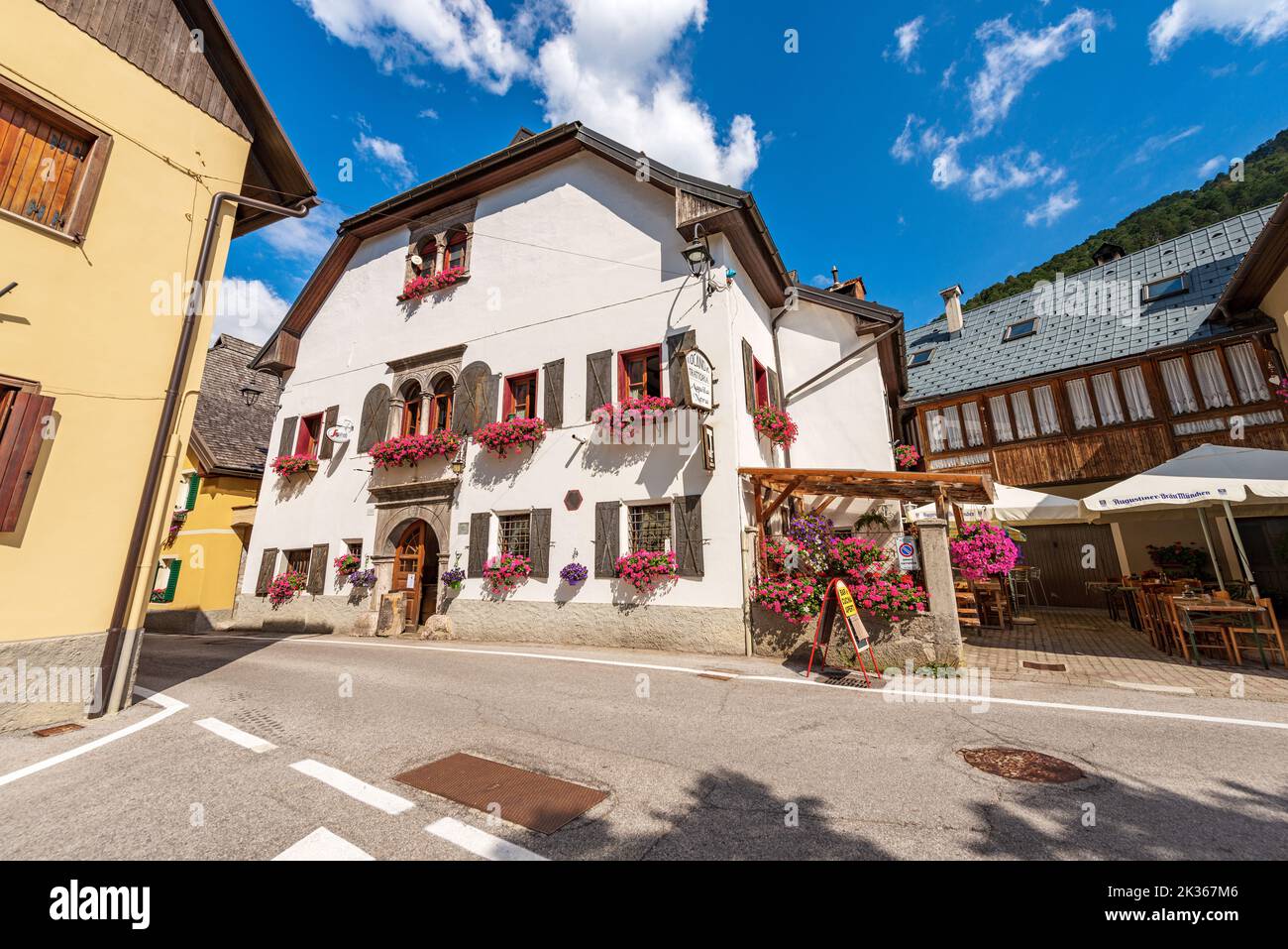 Ancient building with windows with metal shutters and geranium flowers ...