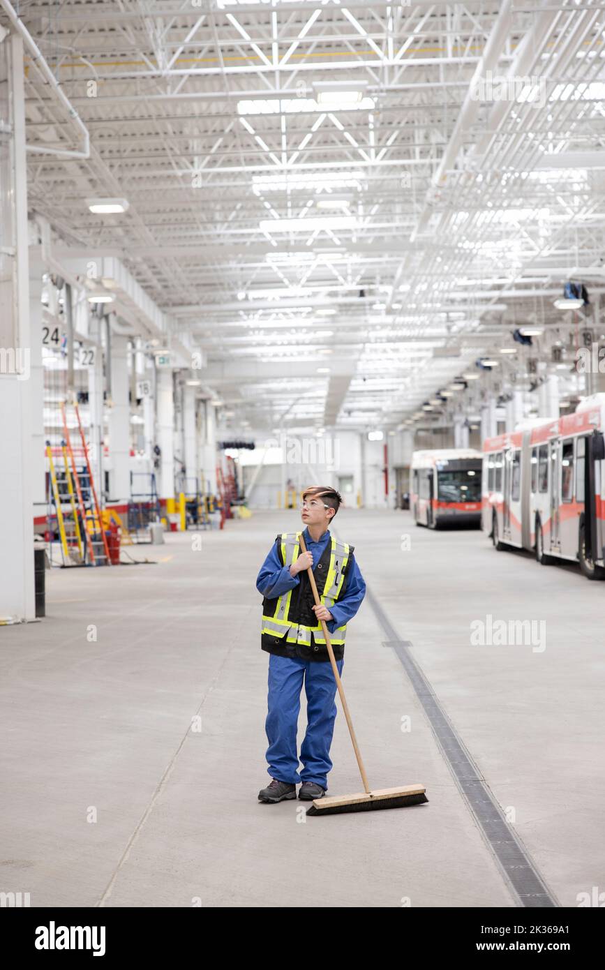 Nonbinary worker with broom in bus maintenance facility Stock Photo - Alamy