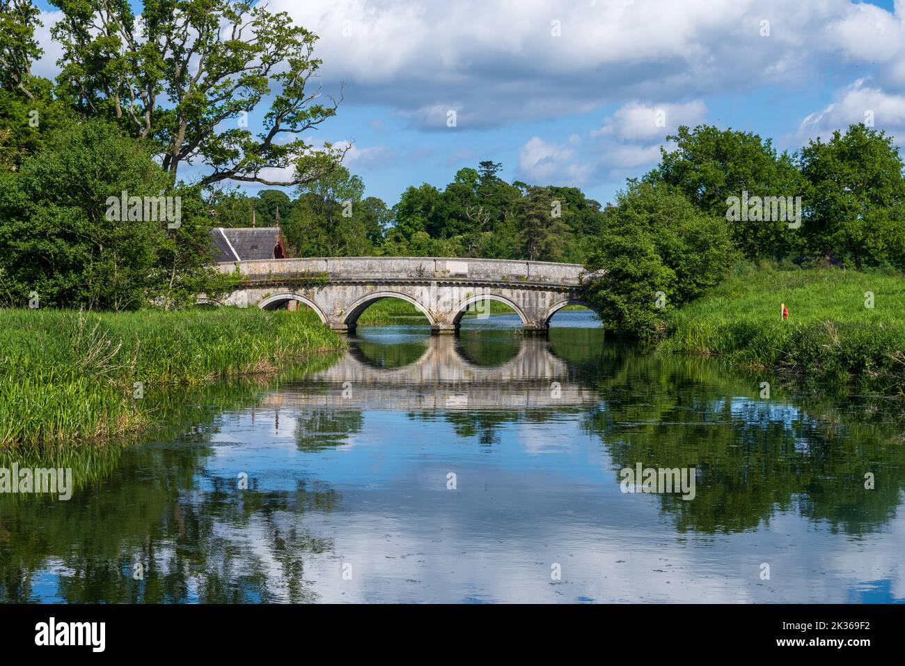 old stone bridge reflecting in a still river in green Irish countryside ...