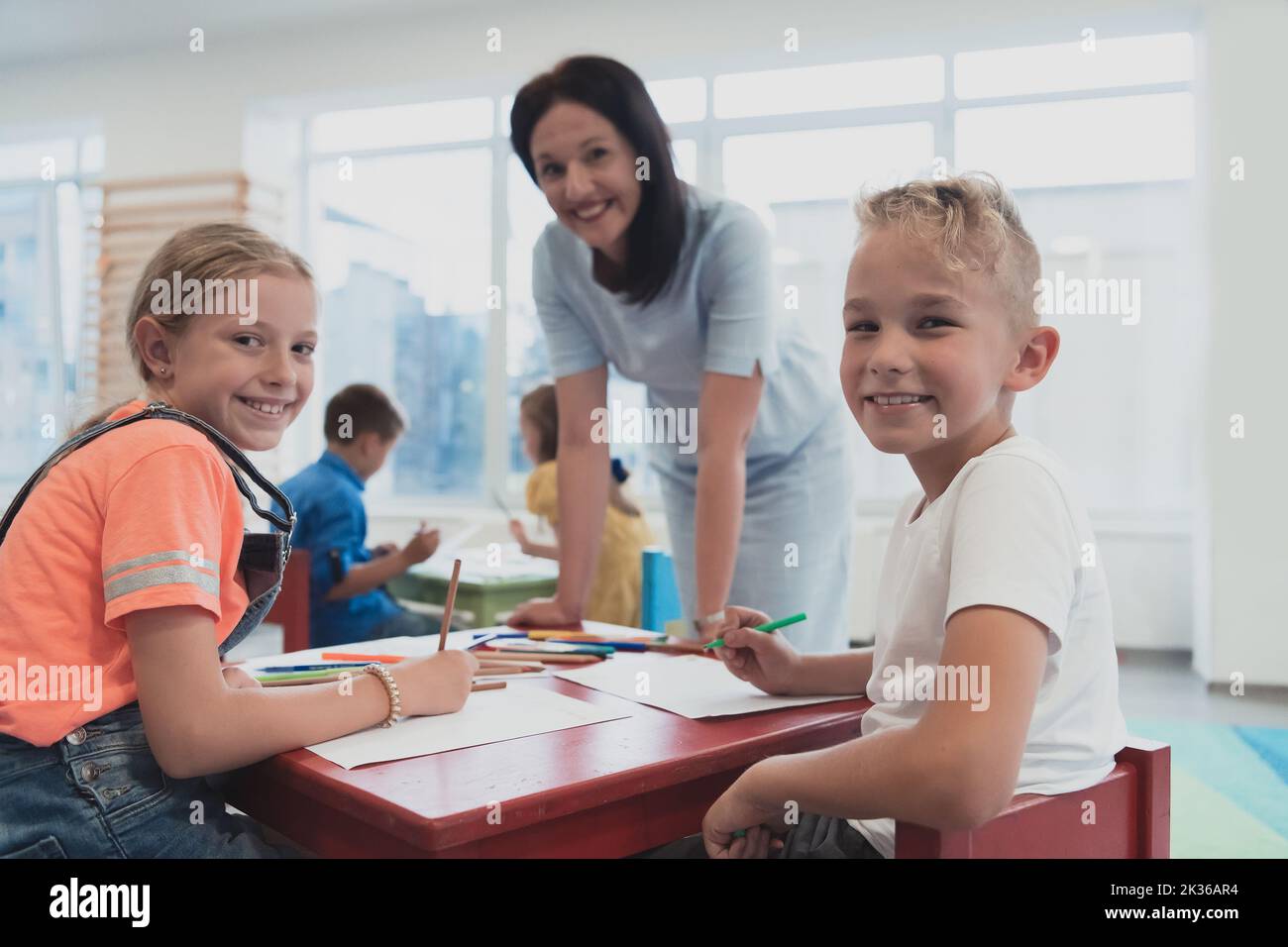 Creative kids during an art class in a daycare center or elementary school classroom drawing ...
