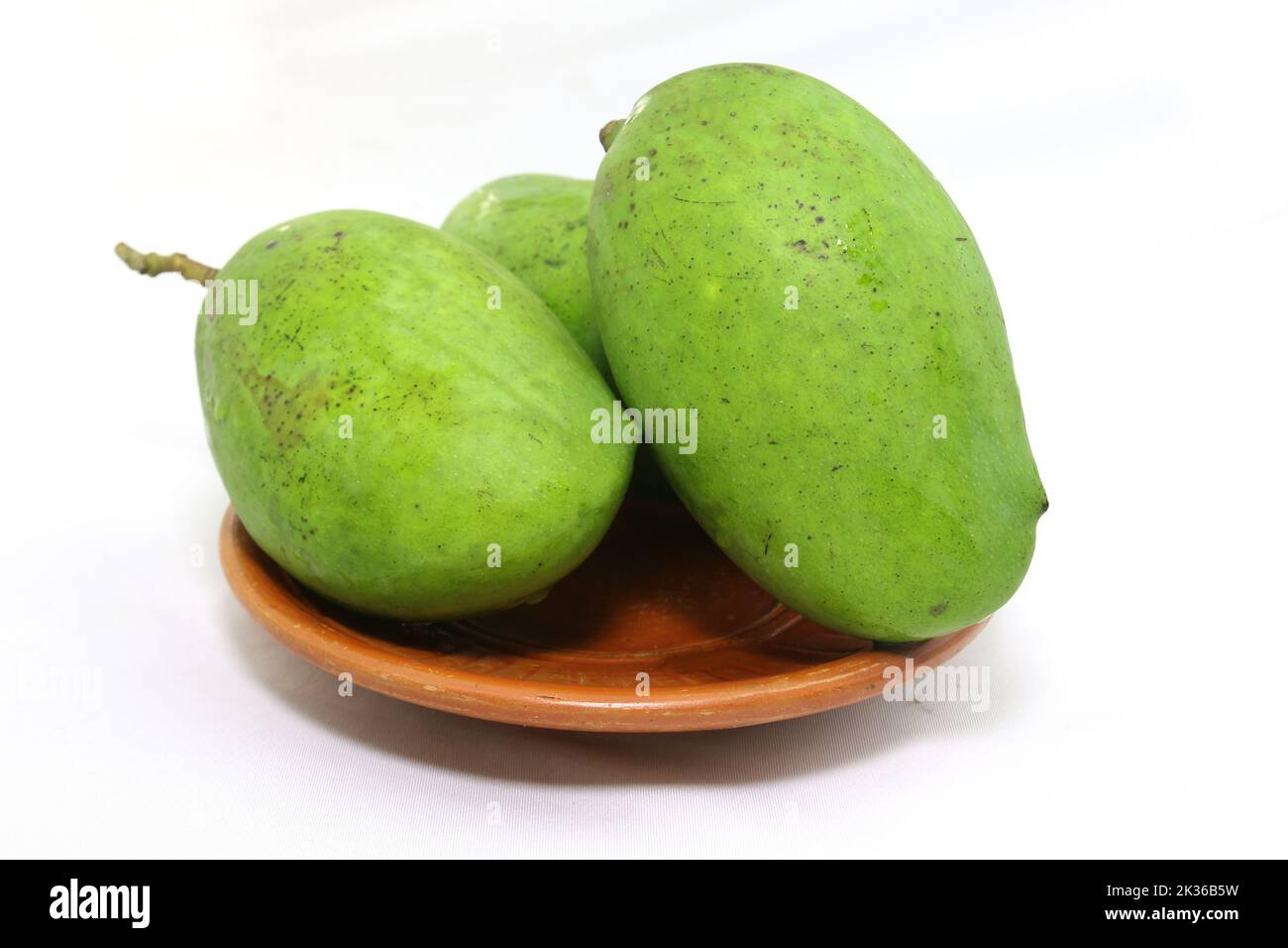 unpeeled green mangoes on clay plate. studio photo shoot. studio photo ...
