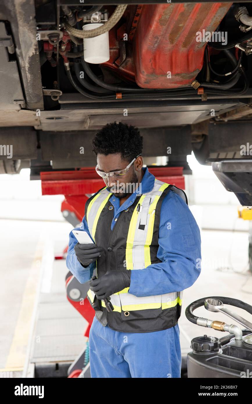 Male mechanic using smart phone under bus in maintenance facility Stock ...