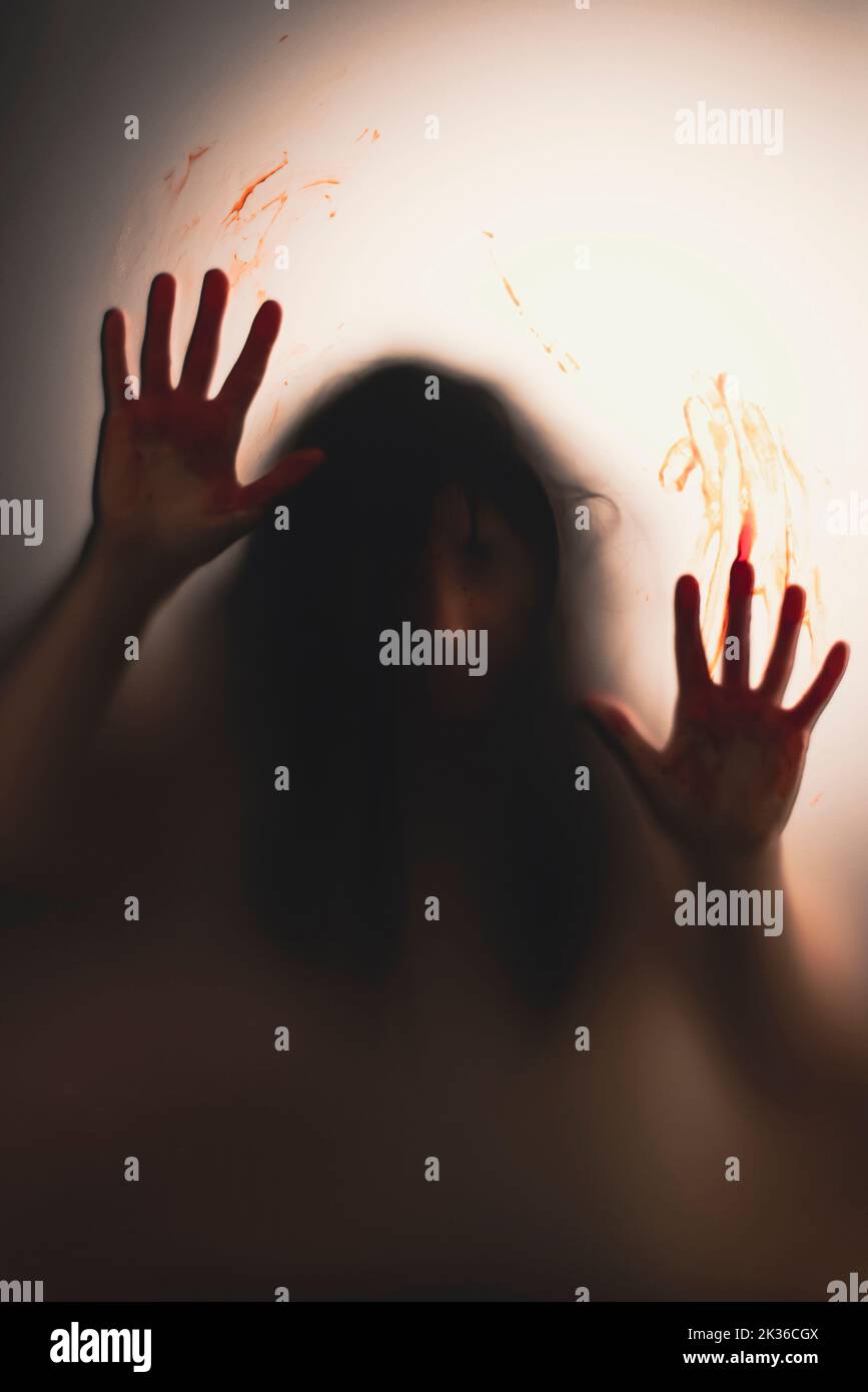 Horror ghost woman with blooded hands behind the matte glass. Halloween ...