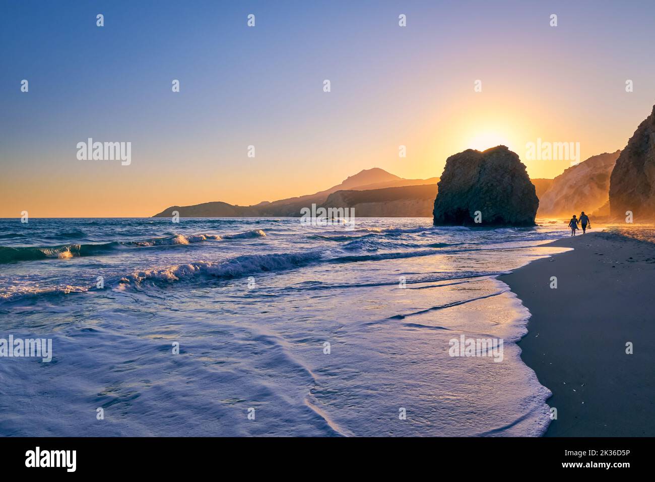 Silhouettes of two adults walking in tide, beach on sunset, Milos ...