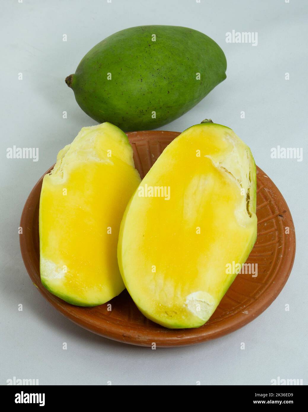 unpeeled green mango and sliced mango on clay plate. these mangoes ...