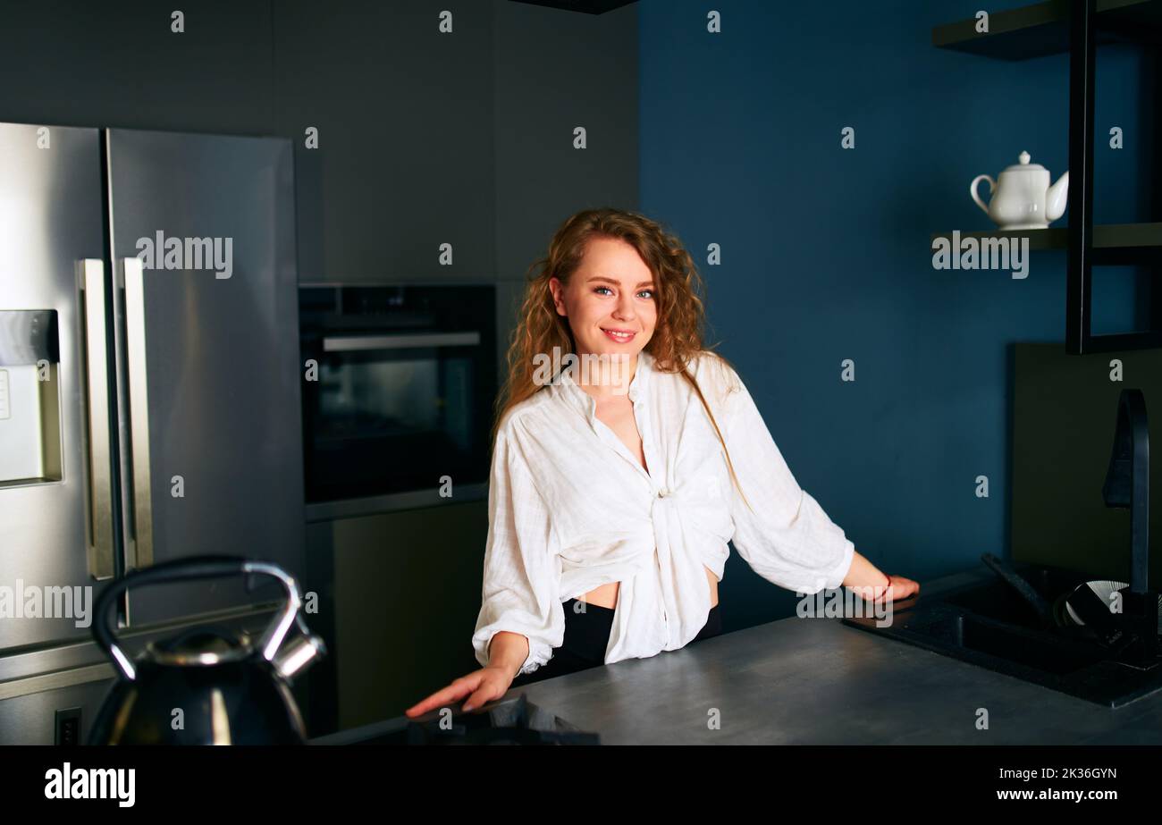 Portrait of blonde caucasian woman standing and smiling in her kitchen ...