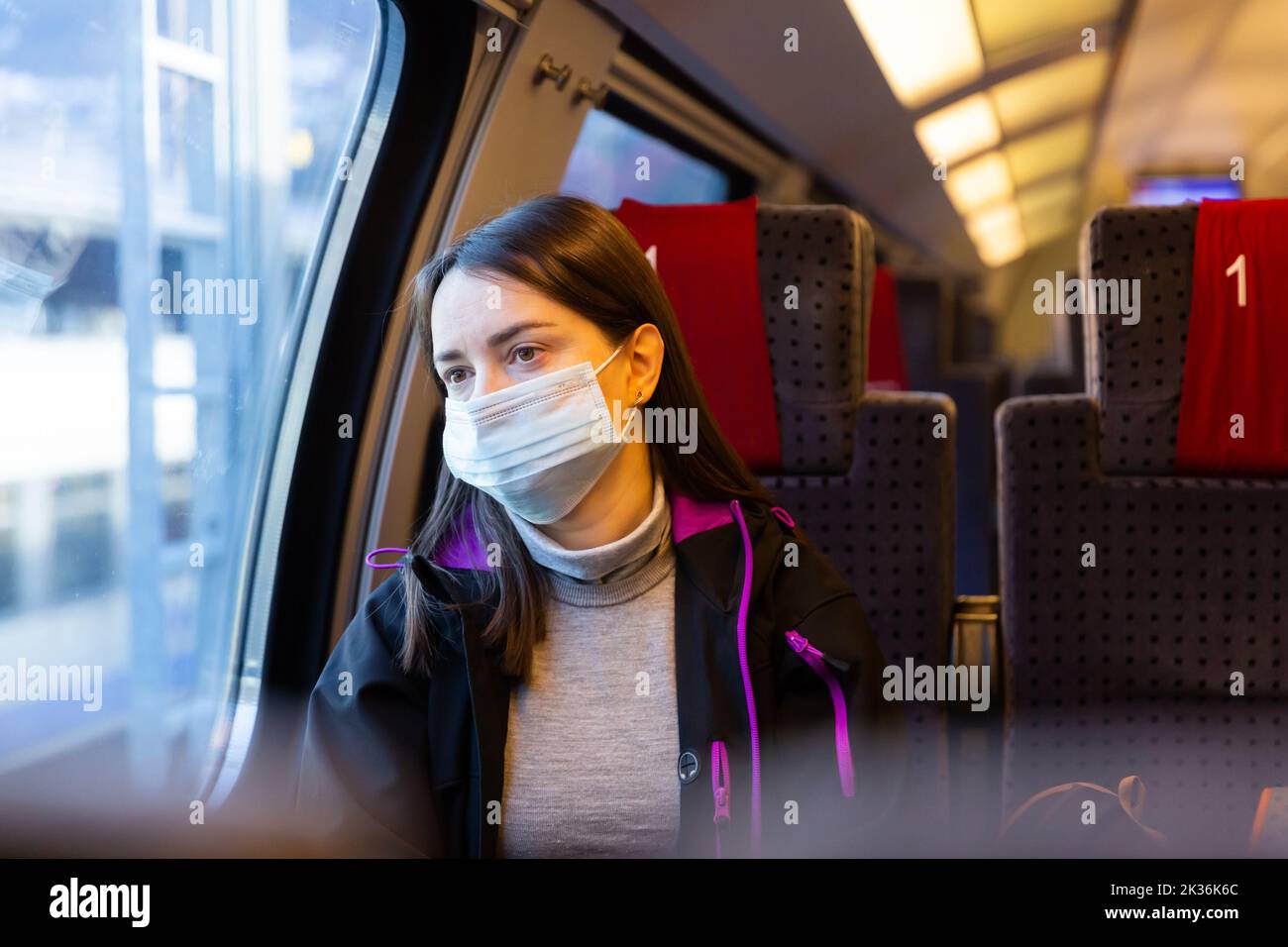 Woman traveler in mask sitting inside train and looking out window ...