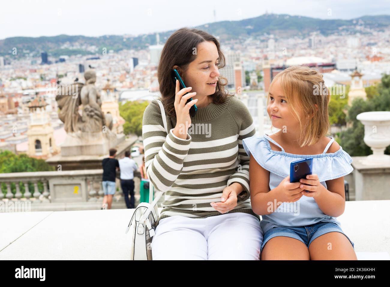 Happy mom with daughter use mobile phones while sitting on parapet Stock Photo - Alamy