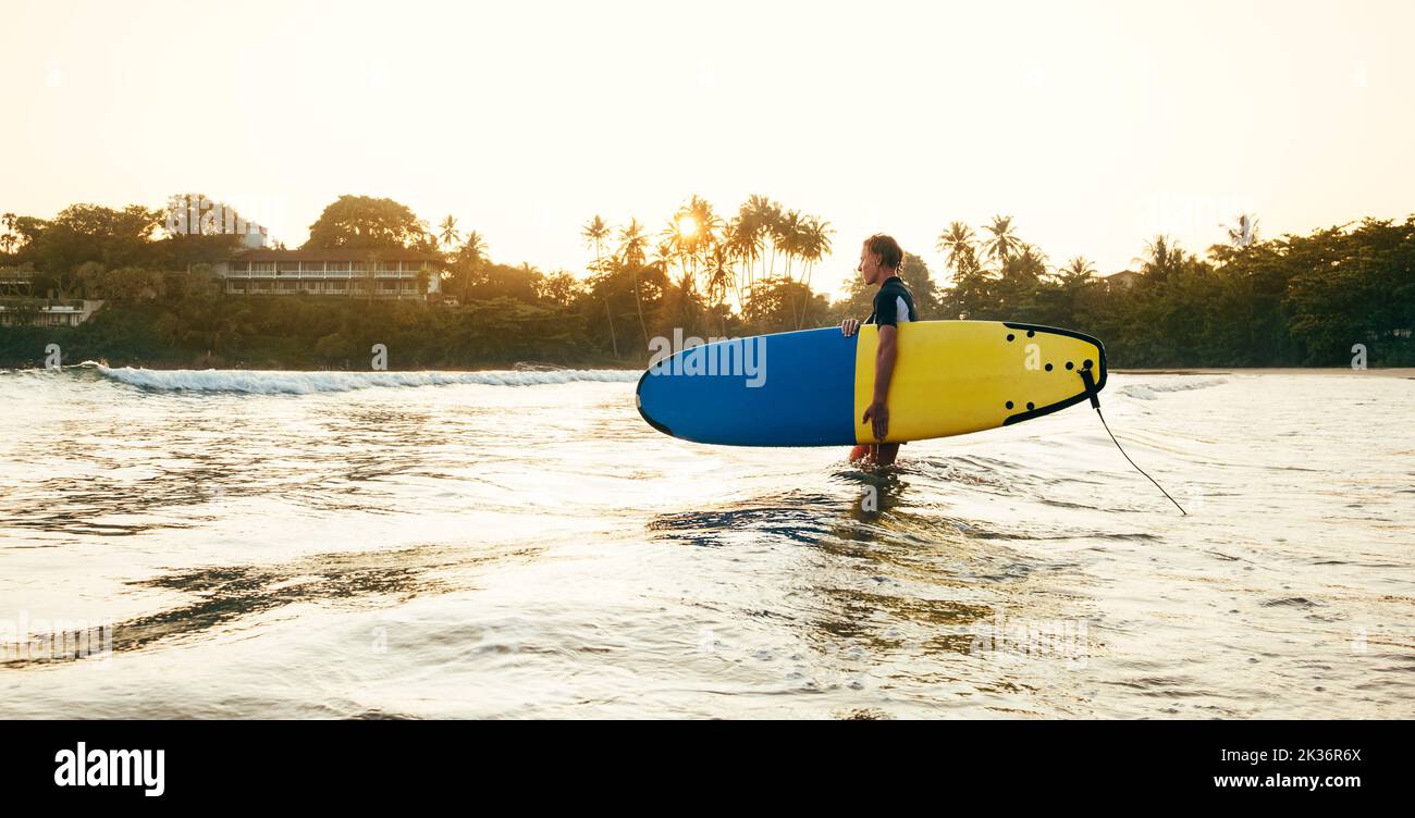 Teen boy with blue and yellow surfboard entering the waves for surfing ...