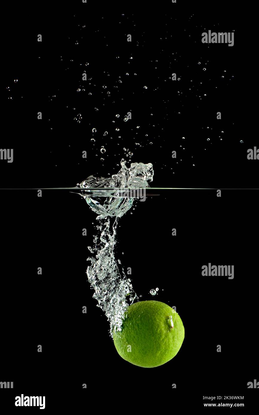 A vertical shot of a green lime dropping into the water with splashes ...