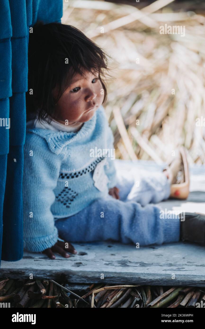 Vertical shot of child sitting on floor of Uros Island, Peru. Uru or ...