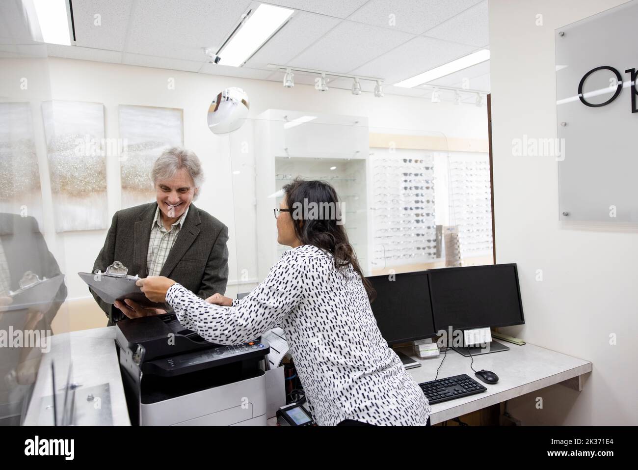 Receptionist explaining paperwork to patient in optometry center Stock ...