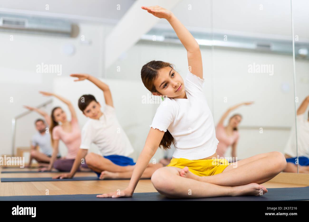 Girl doing stretching in Padmasana pose with brother and parents in ...