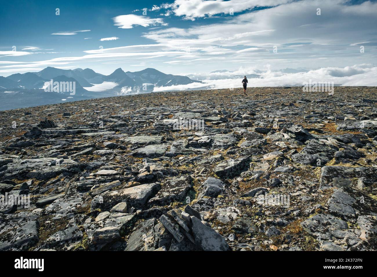 Female hiker coming to the top of stony mountain with clouds and vast ...