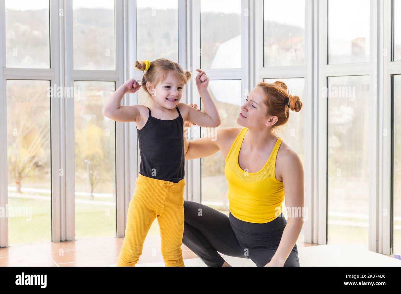 Young fit mom and her daughter in matching clothes, showing muscles ...