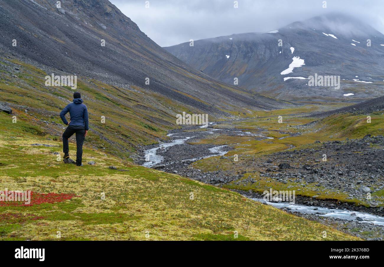 Female hiker overlooking wild river in harsh, remote arctic valley on a ...