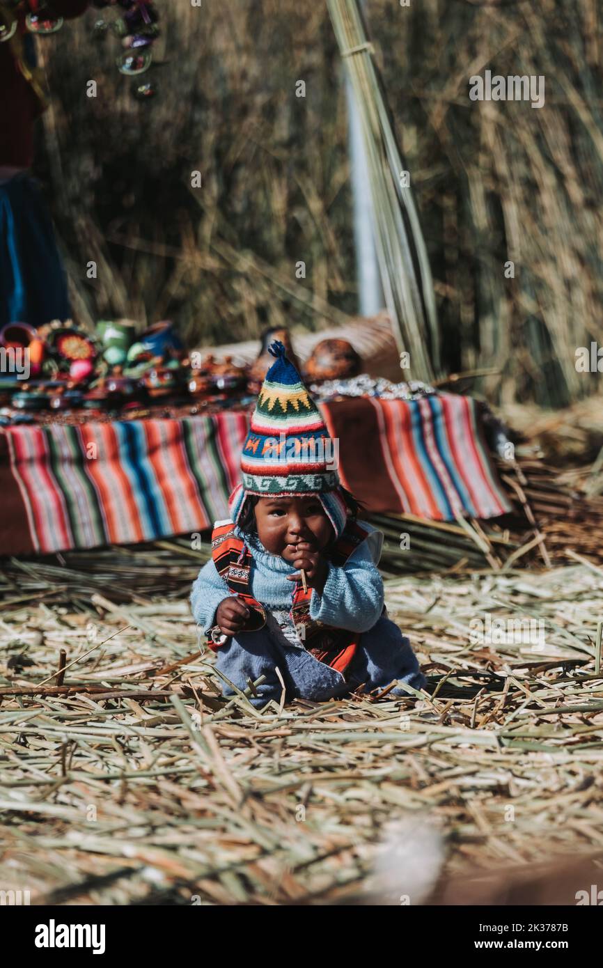 A vertical shot of child sitting on dry bamboo plants of Uros Island ...