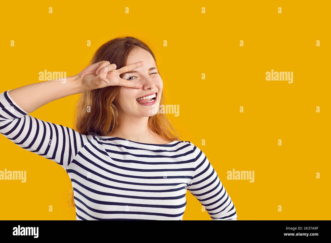 Funny woman smiles, winks her eye, sticks her tongue out and does peace ...