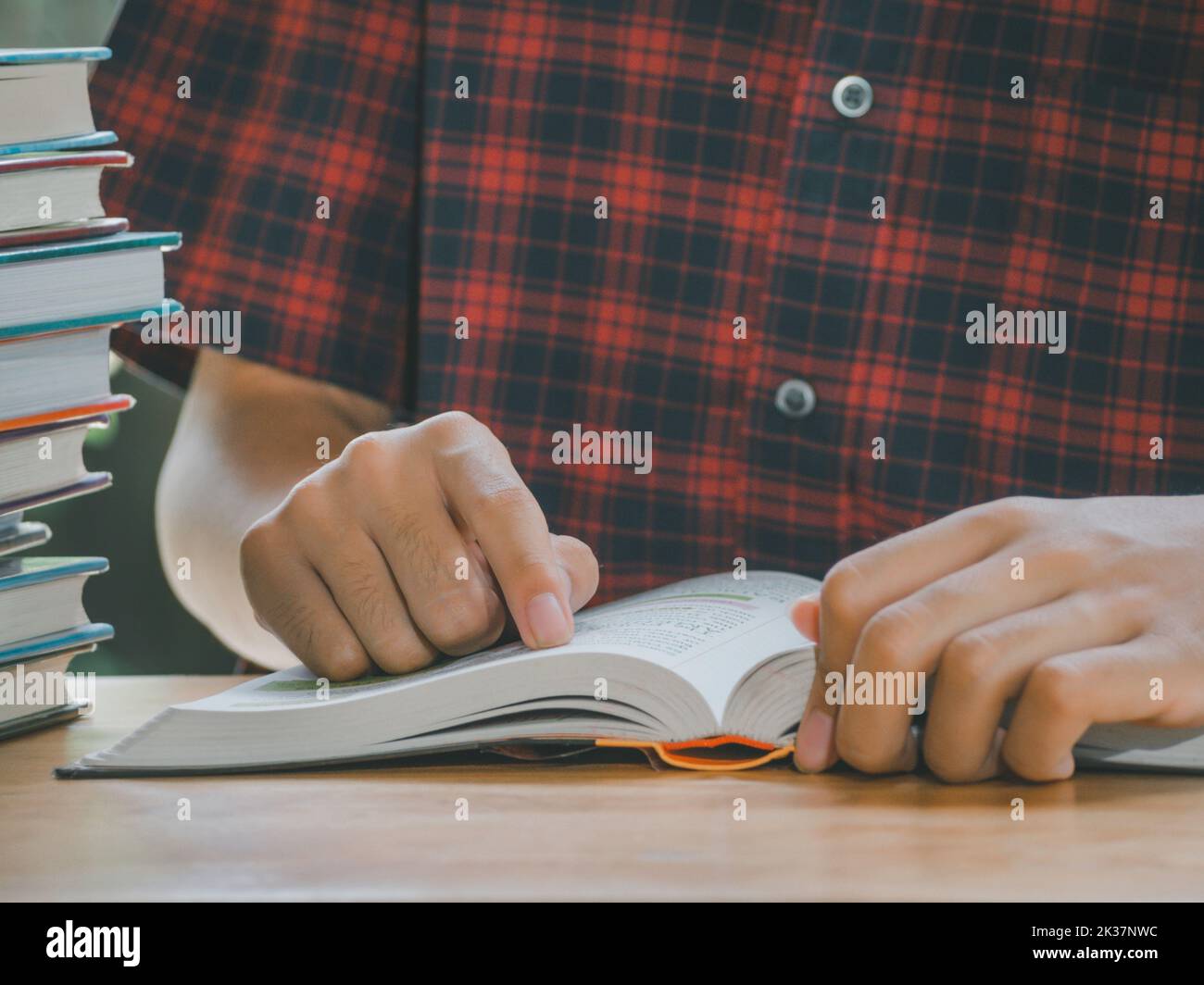 Asian young man opening and reading and pointing a book near book piles ...