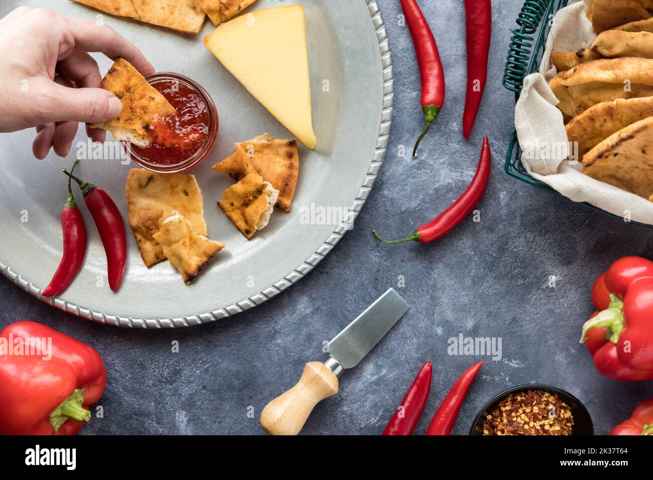 A hand dipping a piece of crisp cracker bread into a jar of hot pepper ...