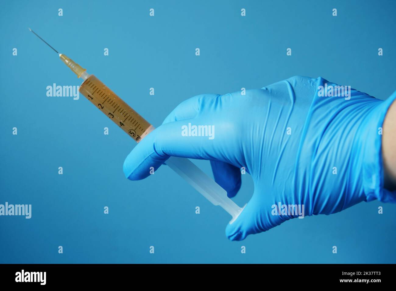 nurse hand in latex glove holding syringe wth orange liquid medicine ...