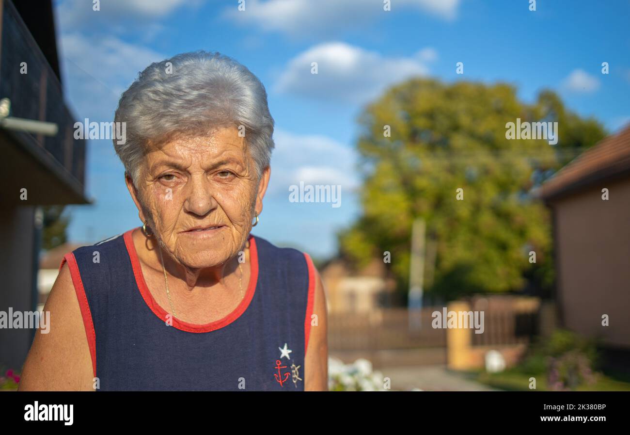 An old grandmother poses in the yard of a country house. her face and ...