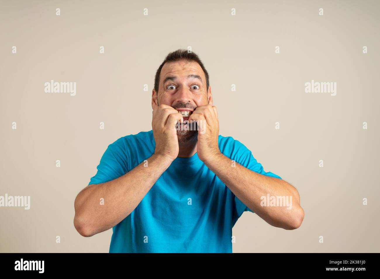 Studio portrait of scared and shocked dark-haired mature man biting his ...