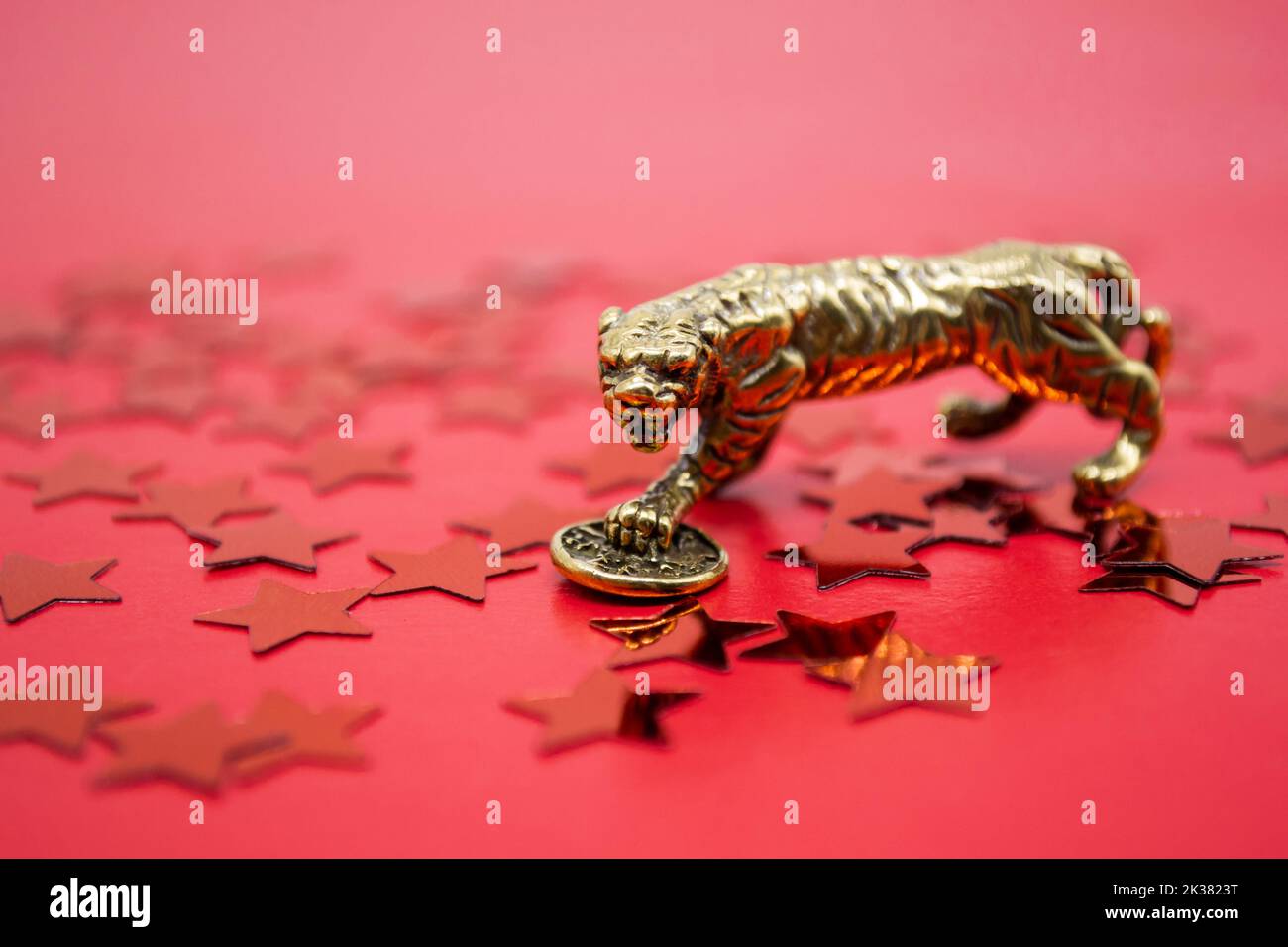 Bronze figure of a tiger with coin on a red background with red stars ...
