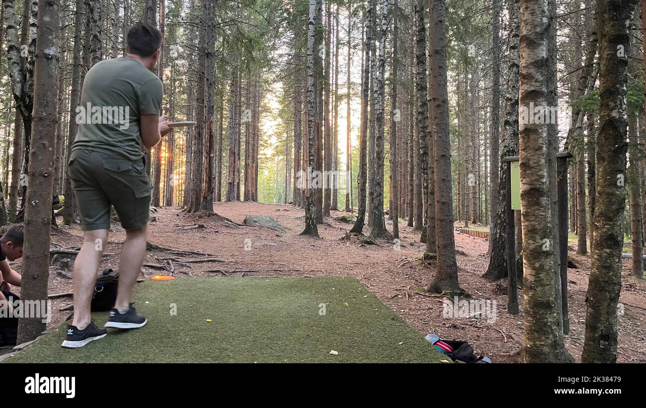 A man playing disc golf in the forest in Norway with a beautiful ...