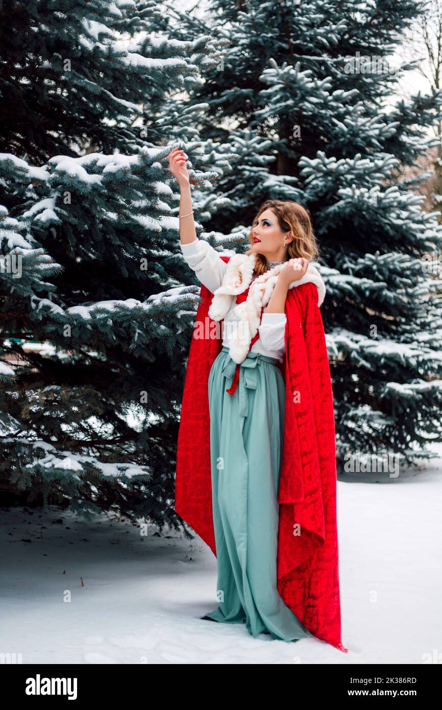 Beautiful woman in a red cloak in a snow-covered coniferous forest ...
