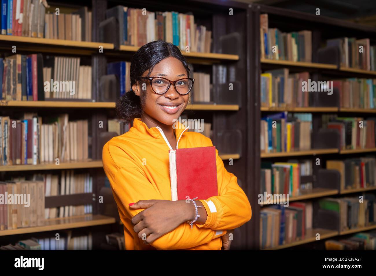 A Black female student holding a red book and standing in the college ...