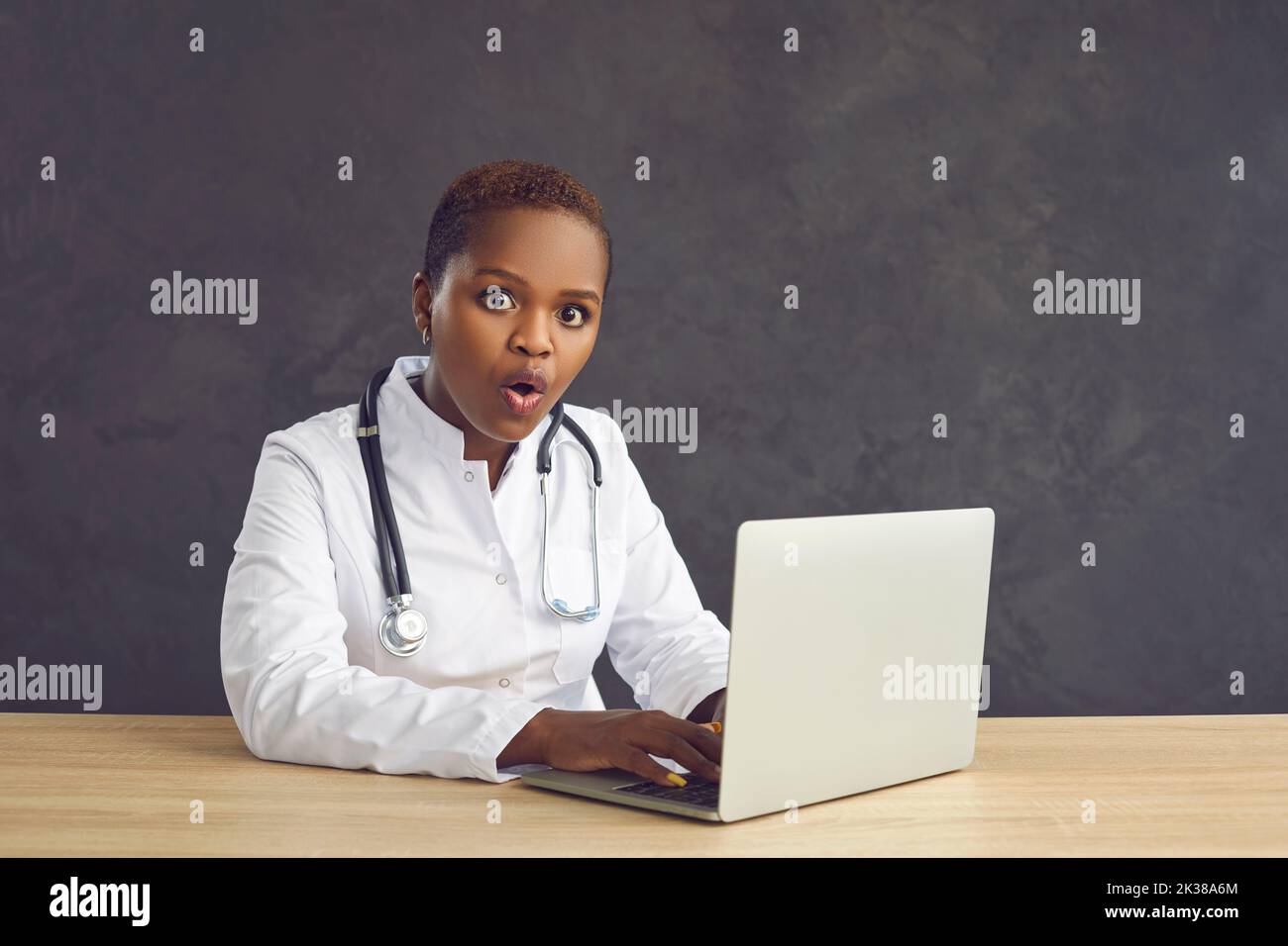Dark skinned female doctor with shocked face sitting at the table on a ...