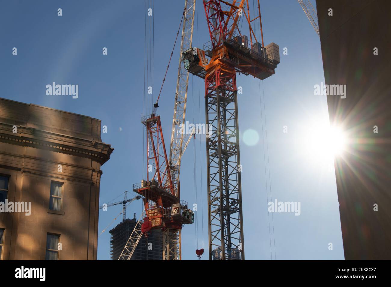The sun shines on large construction cranes building office buildings ...
