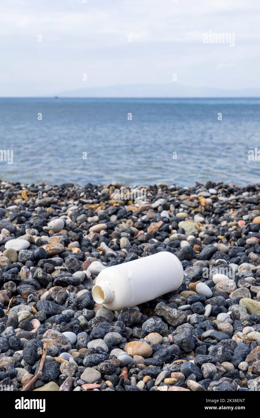 A vertical shot of an empty plastic bottle on a pebble beach, the ...