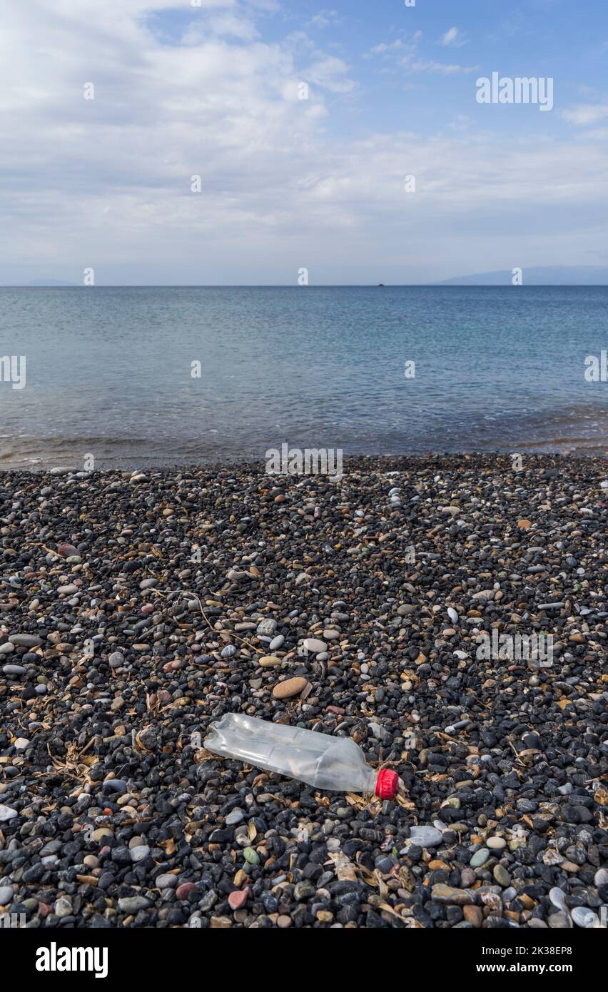 A vertical shot of an empty plastic bottle on a pebble beach, the ...