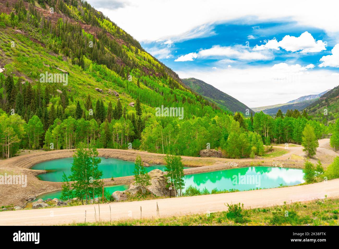 A scenic landscape of a forest on the hill with an emerald green pond ...