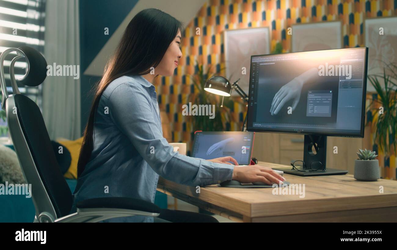 Asian woman sitting on chair at the table at home office and making 3D prototype of human hand ...