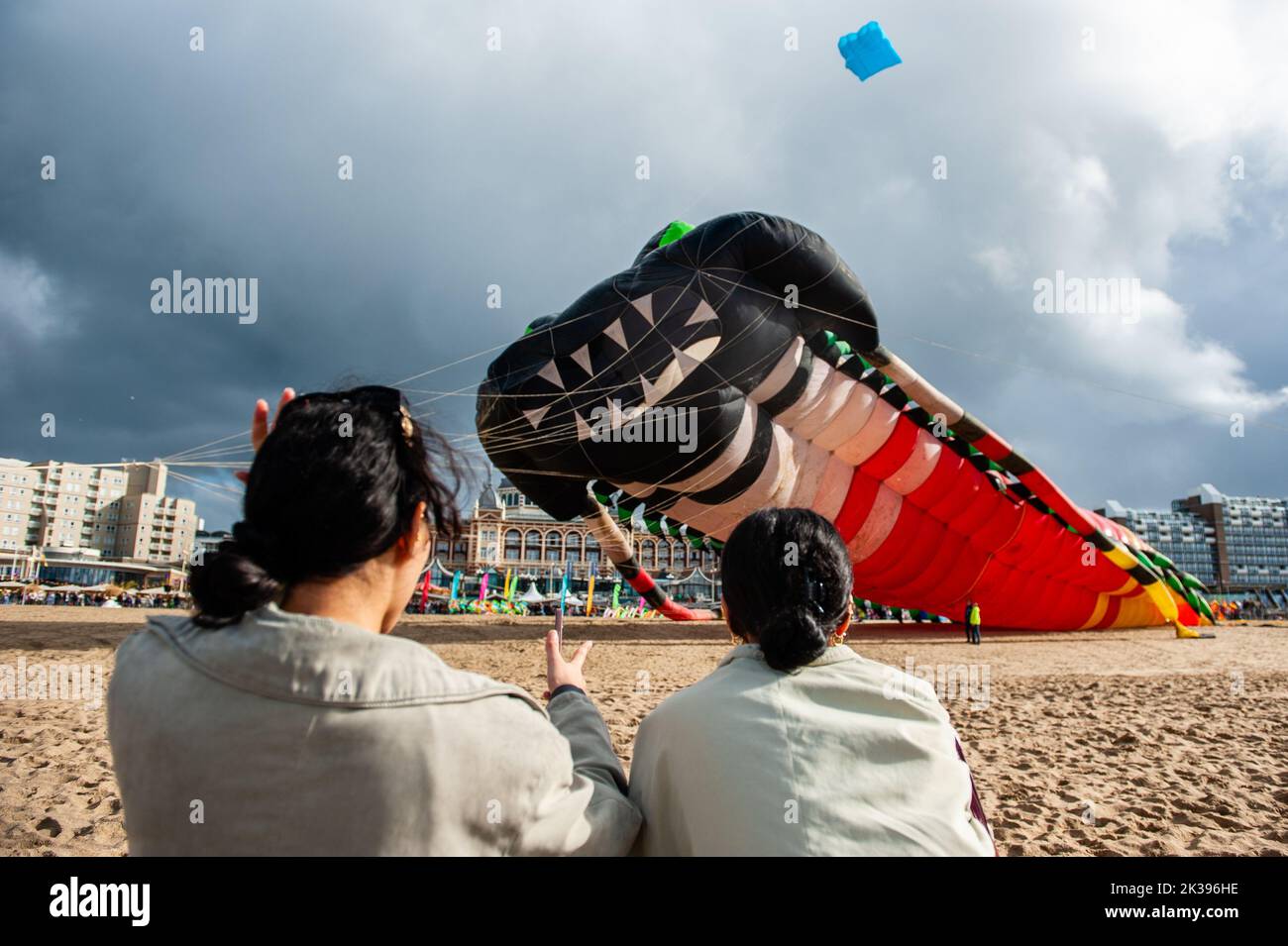 Two women observe the huge kite trying to fly in the sky. The ...