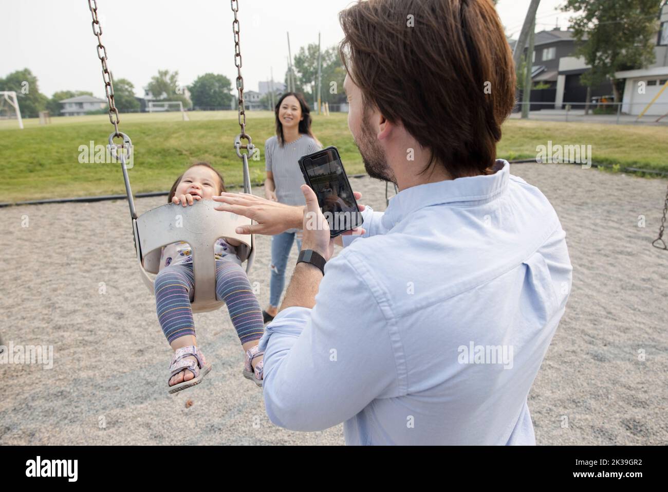 Parents pushing baby daughter on swing at playground Stock Photo - Alamy