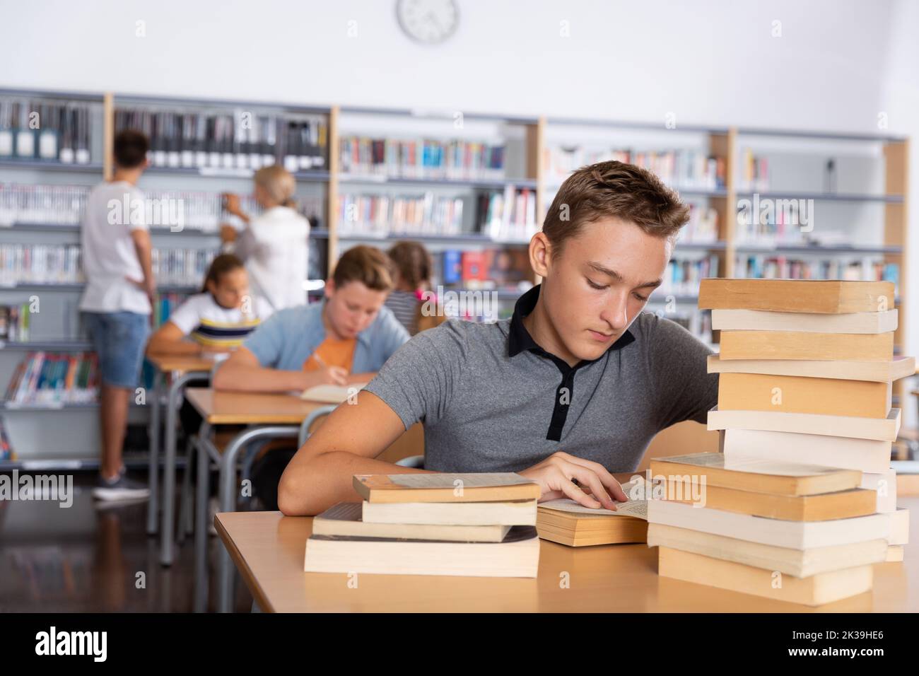 Upset schoolboy sitting with stacks of books in library Stock Photo - Alamy