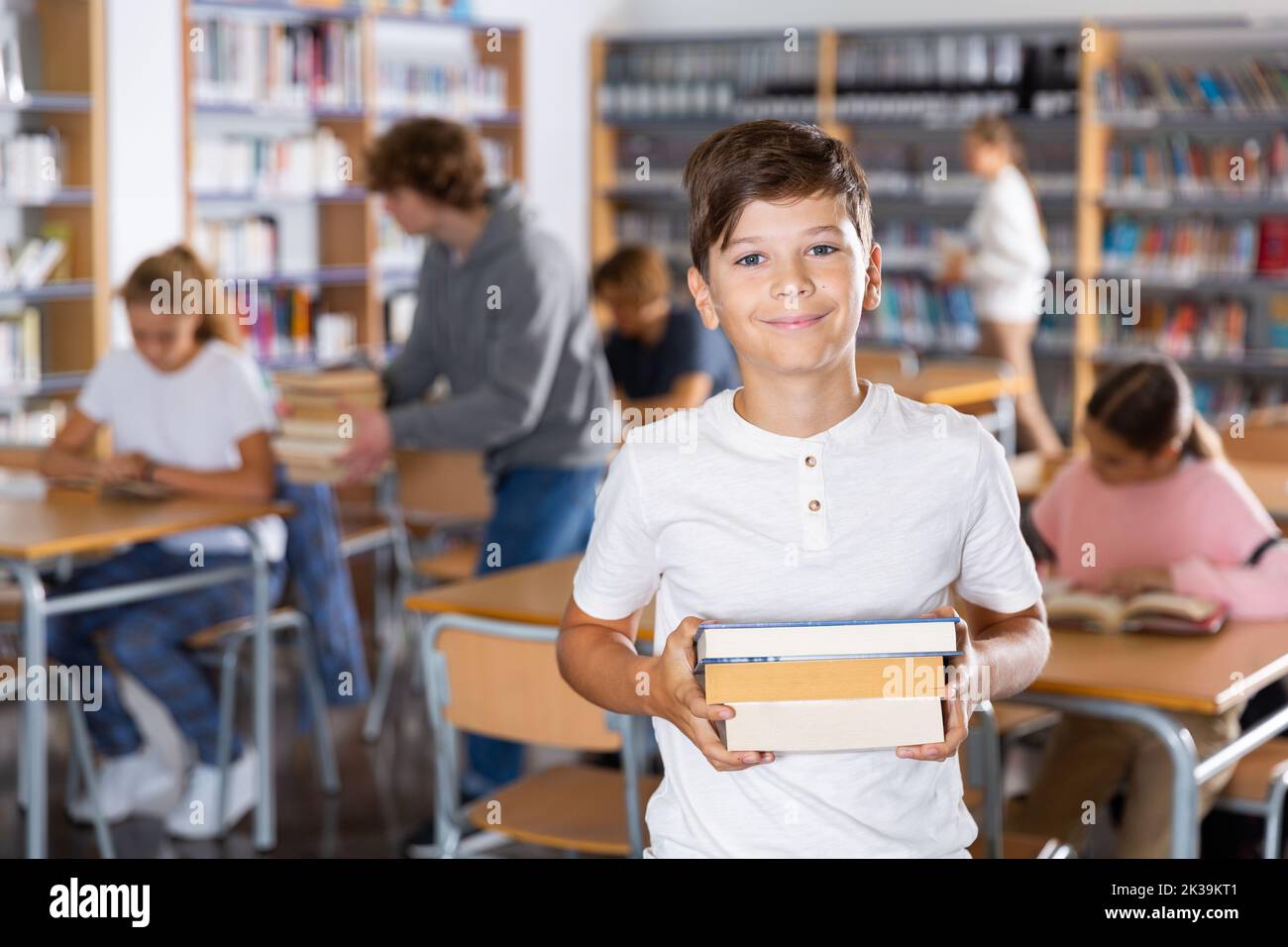Boy with pile of books in library Stock Photo - Alamy