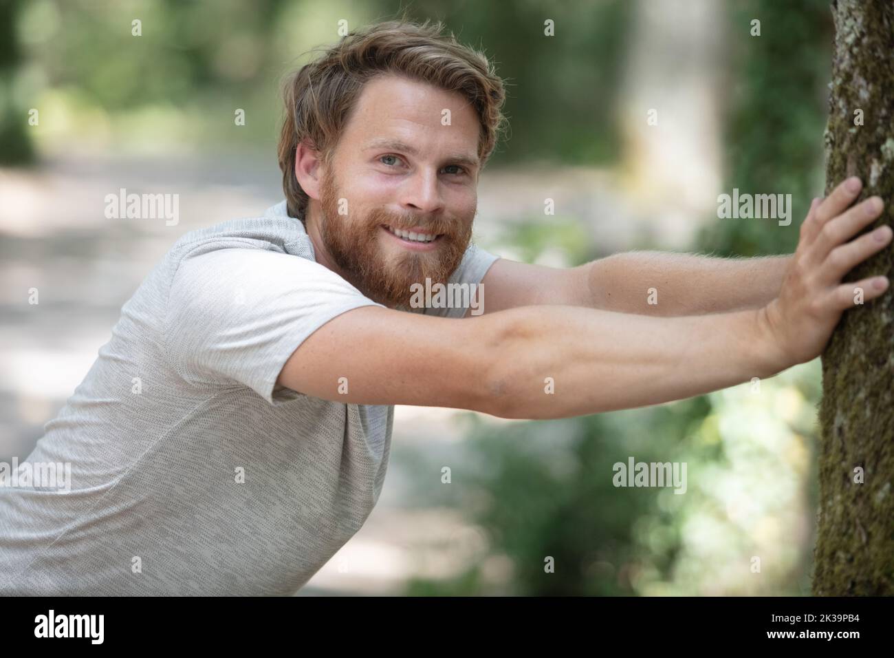 handsome young man leaning against tree pushing it Stock Photo - Alamy
