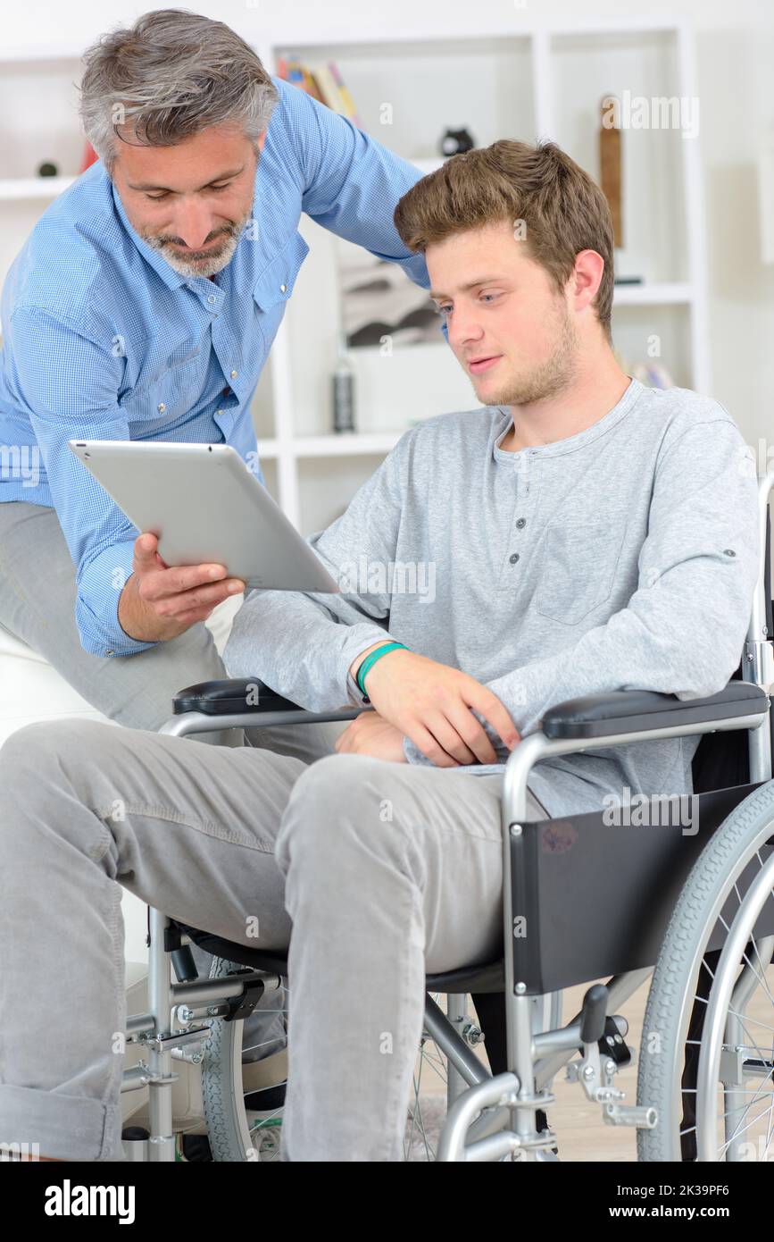 Man showing tablet screen to boy in wheelchair Stock Photo - Alamy