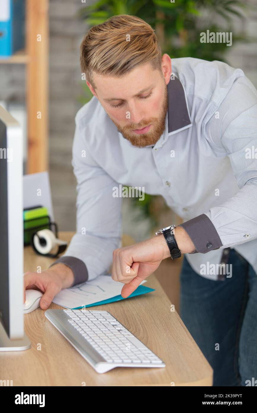 stressed man using computer looks at his wristwatch Stock Photo - Alamy