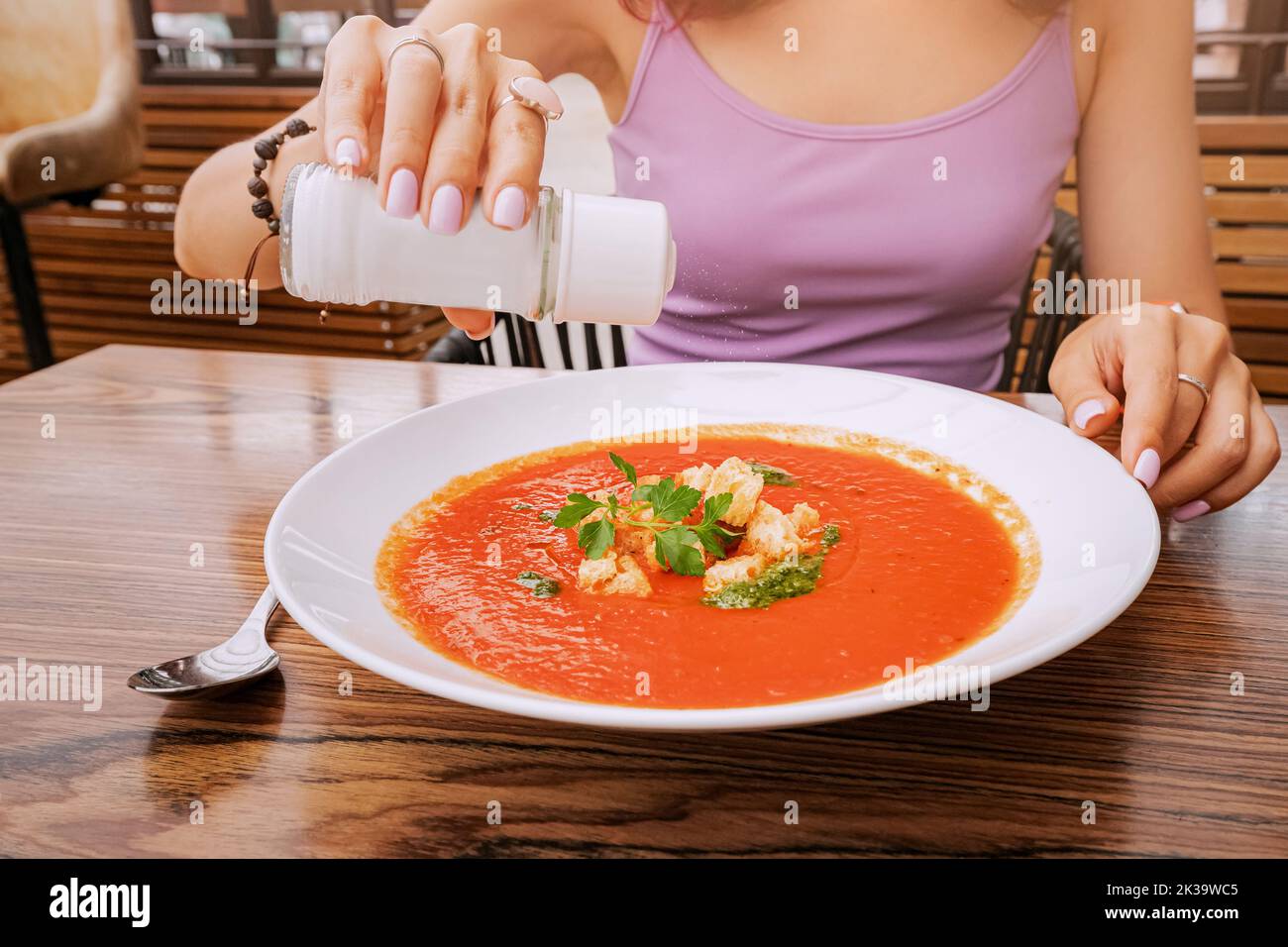 A woman adds salt from a saltcellar to soup in a restaurant. An ...