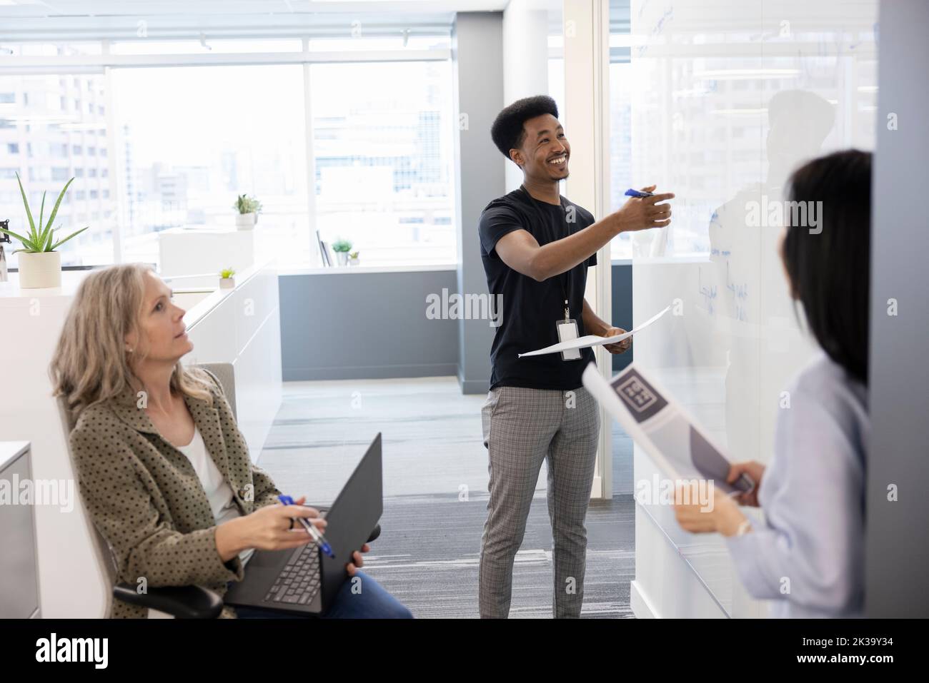 Cheerful apprentice explaining project on whiteboard in team meeting ...